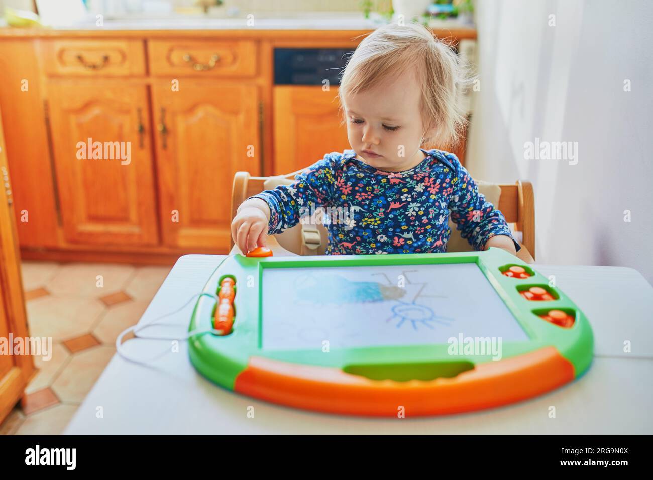 Adorable little girl drawing on magnetic magic screen at home, in ...