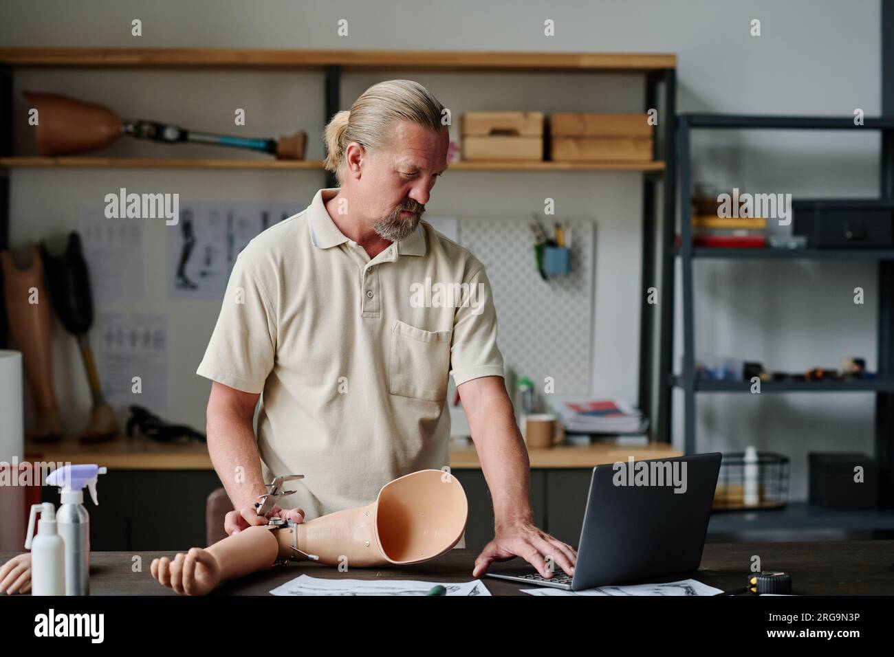 Side view portrait of senior man making arm prosthetics in workshop and ...