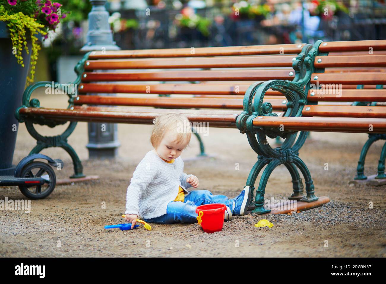 Little baby girl sitting on the ground near bench on a street of ...