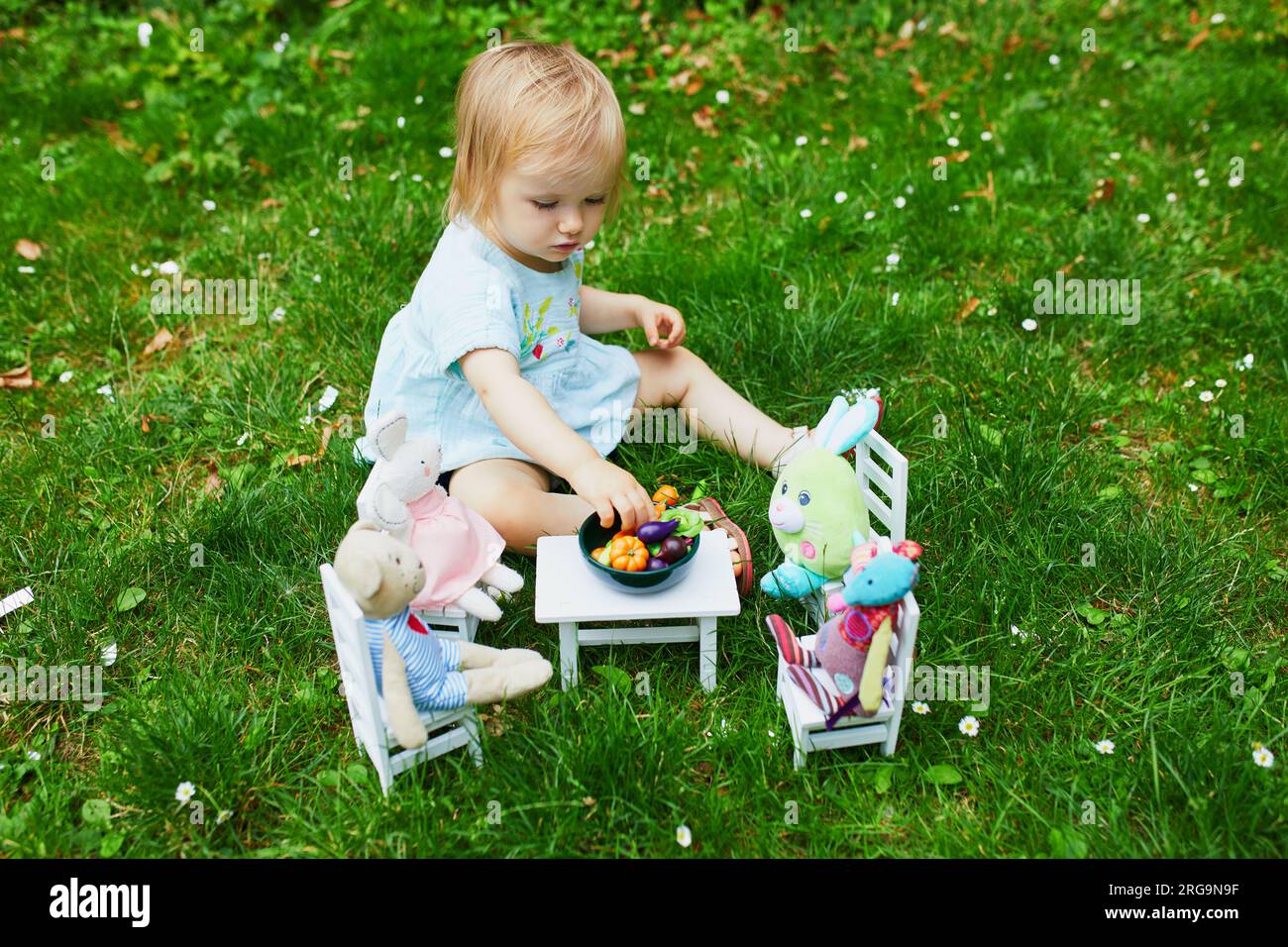 Adorable little girl playing with soft toys in park or garden and ...
