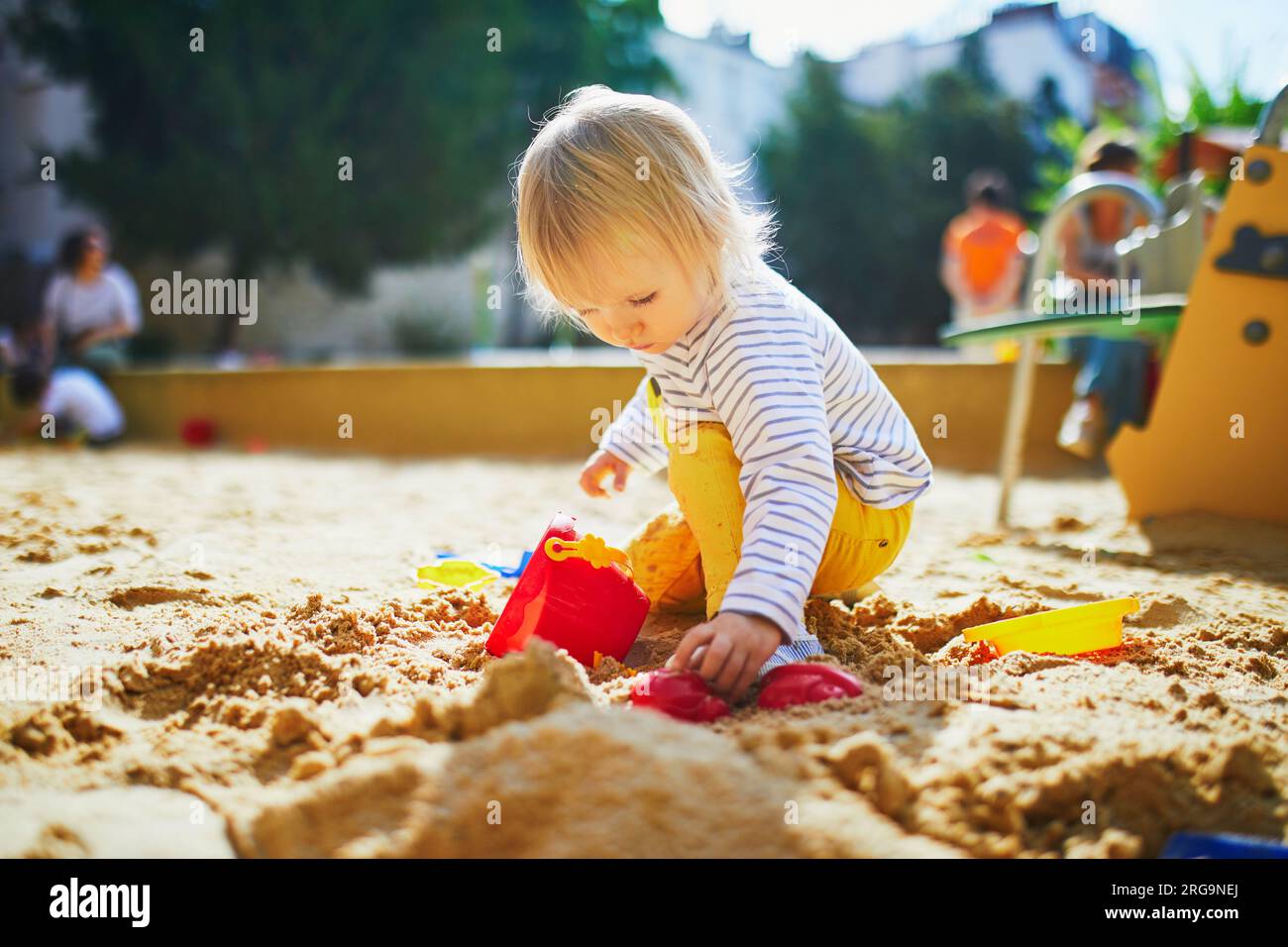 Adorable little girl on playground in sandpit. Toddler playing with sand molds and making ...