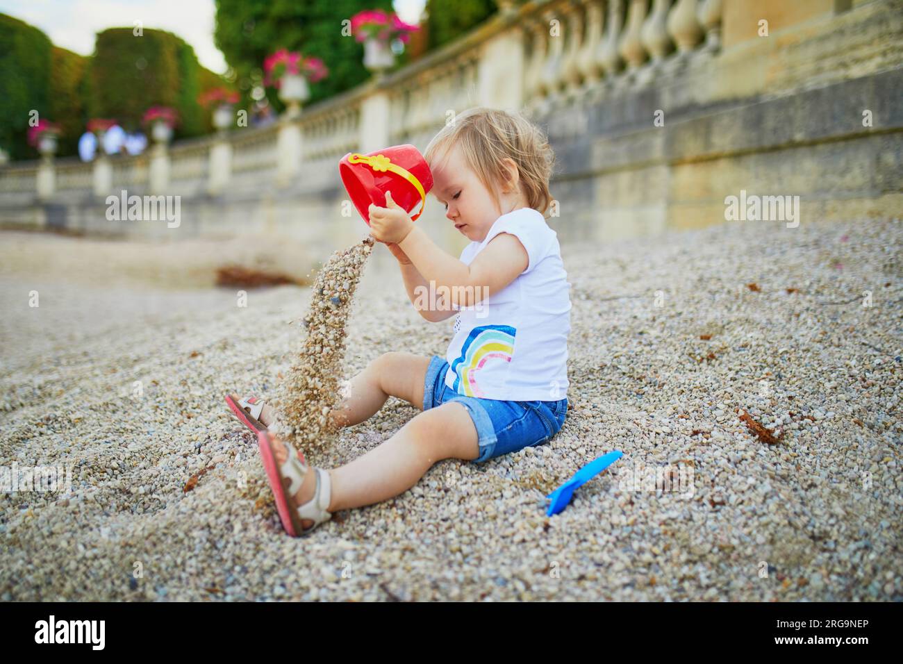 Little girl sitting on a large heap of stones and playing with pebbles ...