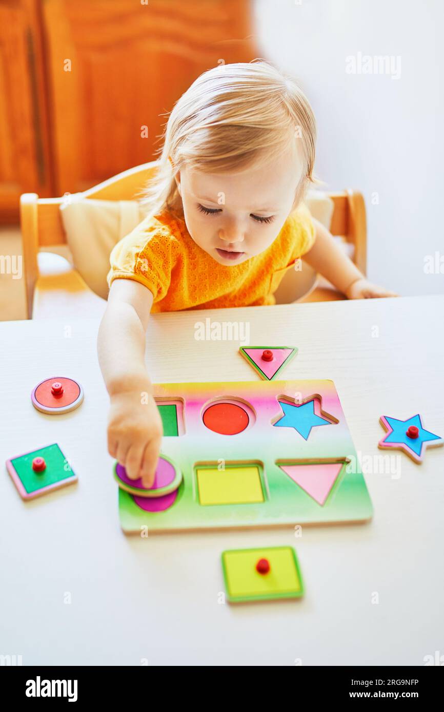 Adorable toddler girl doing wooden puzzle. Child learning geometric ...