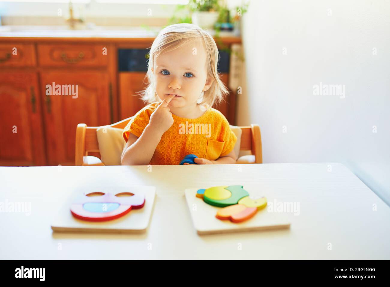 Adorable toddler girl doing wooden puzzle, looking confused, not sure ...