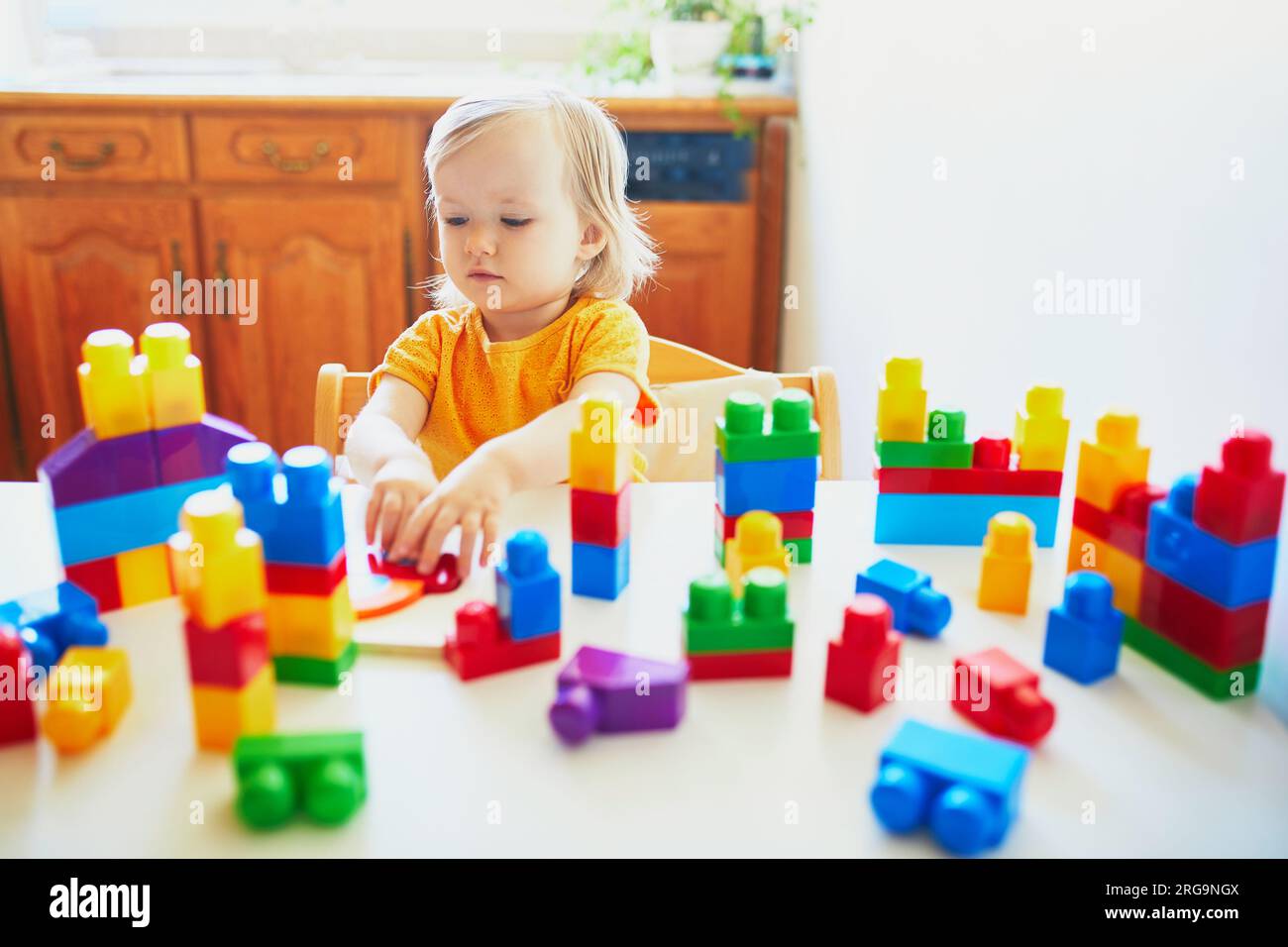 Adorable little girl playing with colorful plastic construction blocks ...