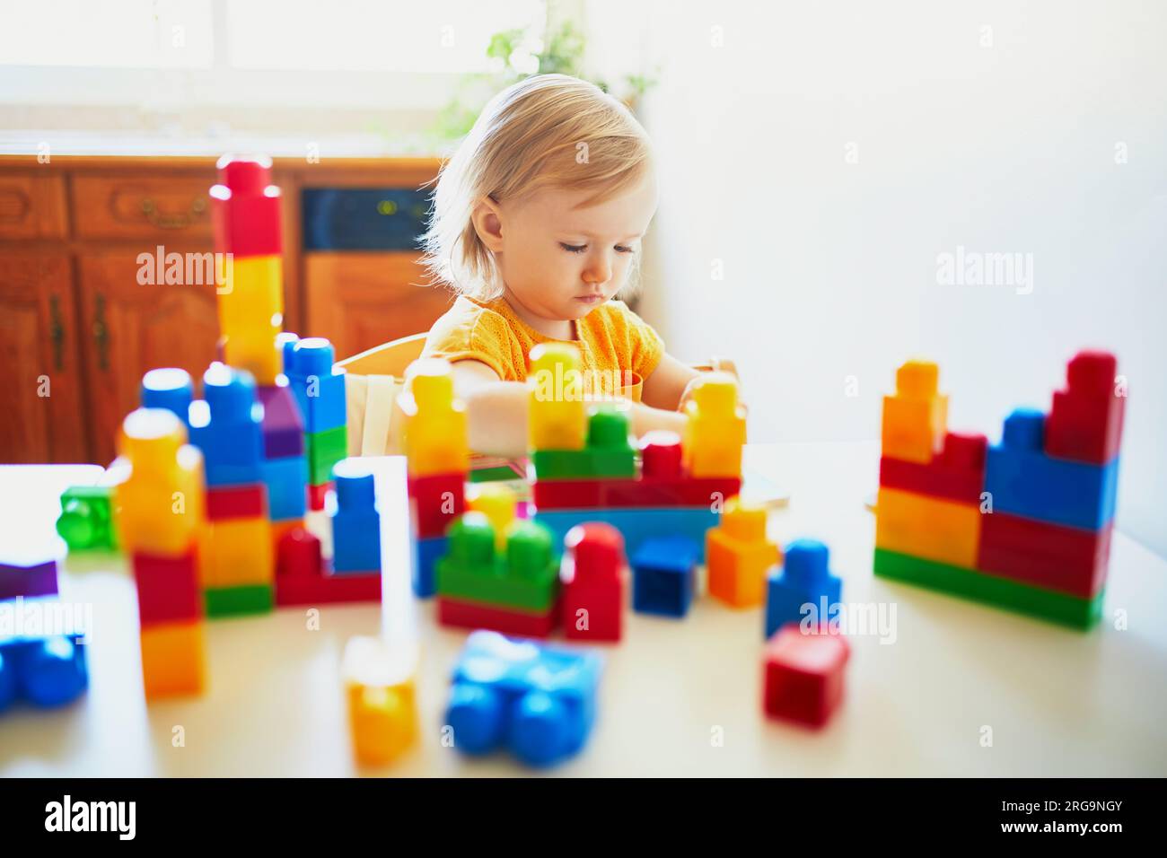 Adorable little girl playing with colorful plastic construction blocks ...