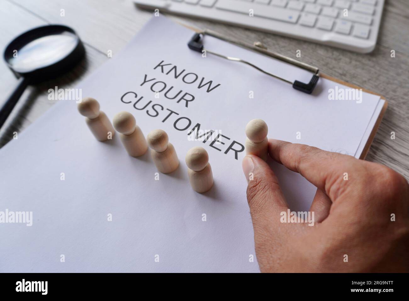 Hand pick wooden doll on paper clipboard with text KNOW YOUR CUSTOMER ...