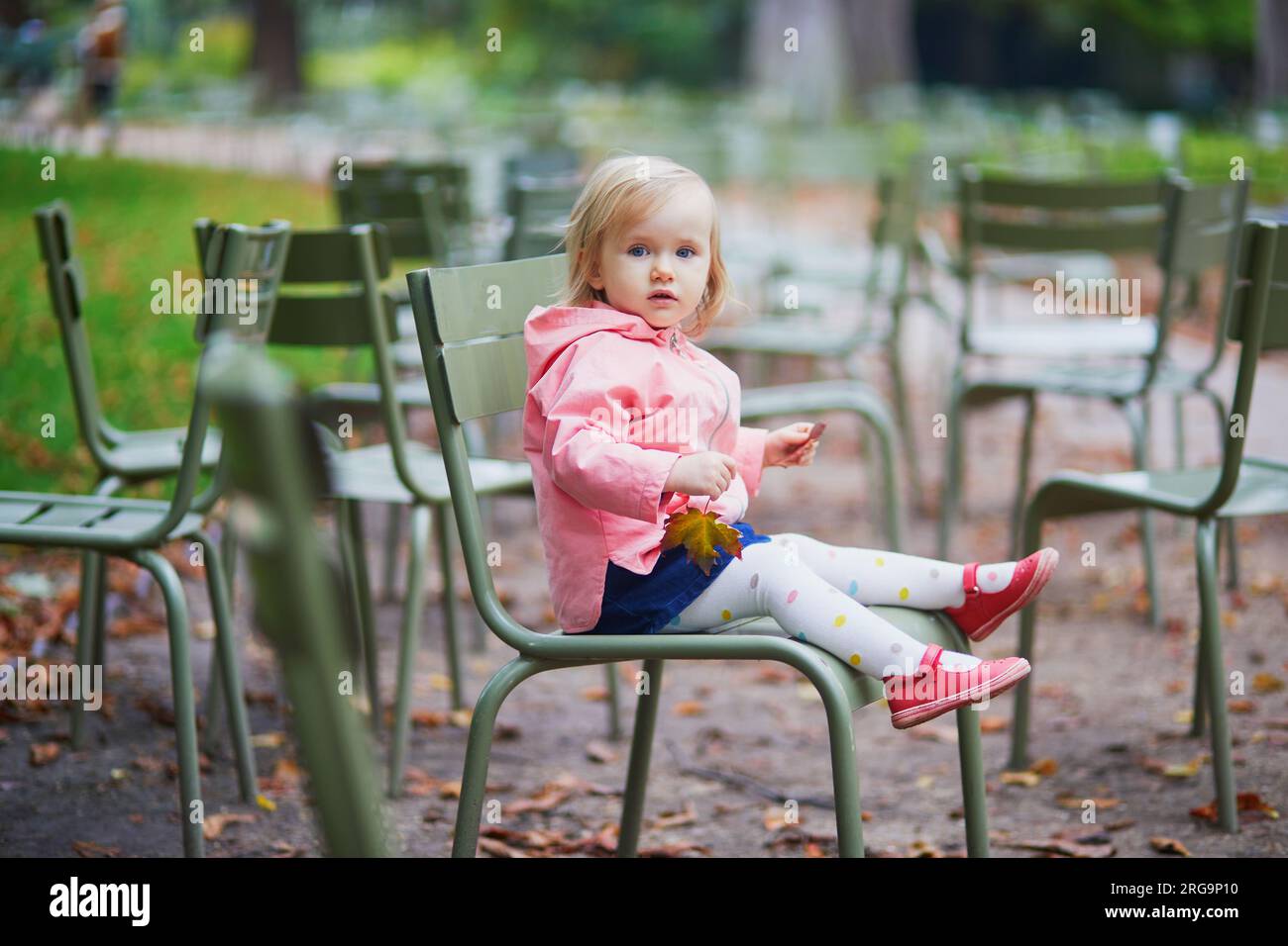 Adorable toddler girl sitting on traditional green chair in Tuileries ...