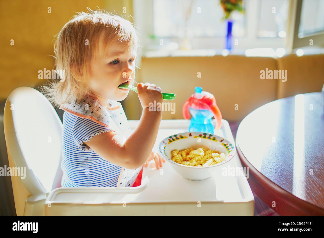 Adorable little girl eating pasta at home. Toddler enjoying her food ...
