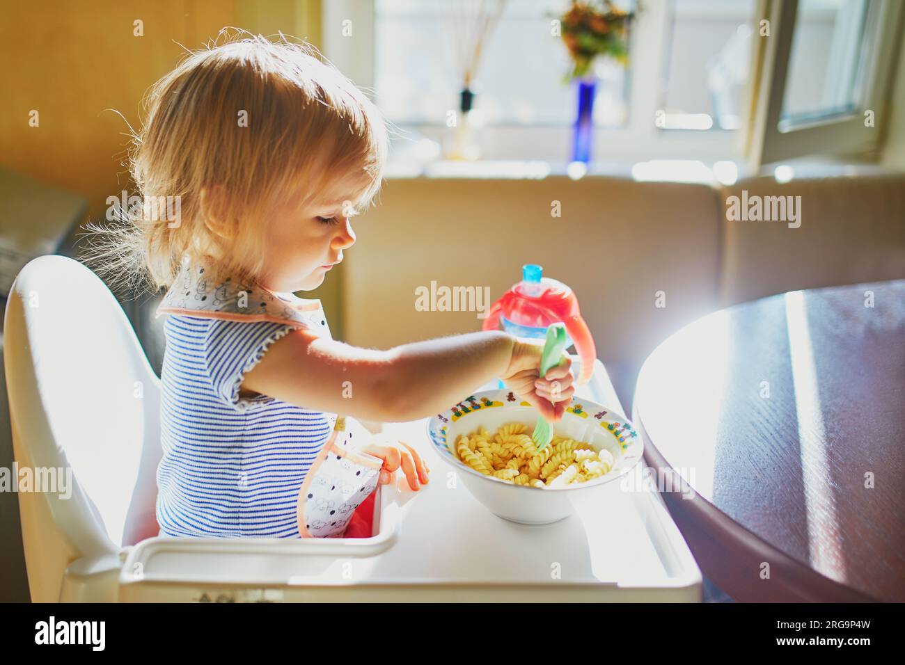 Adorable little girl eating pasta at home. Toddler enjoying her food ...