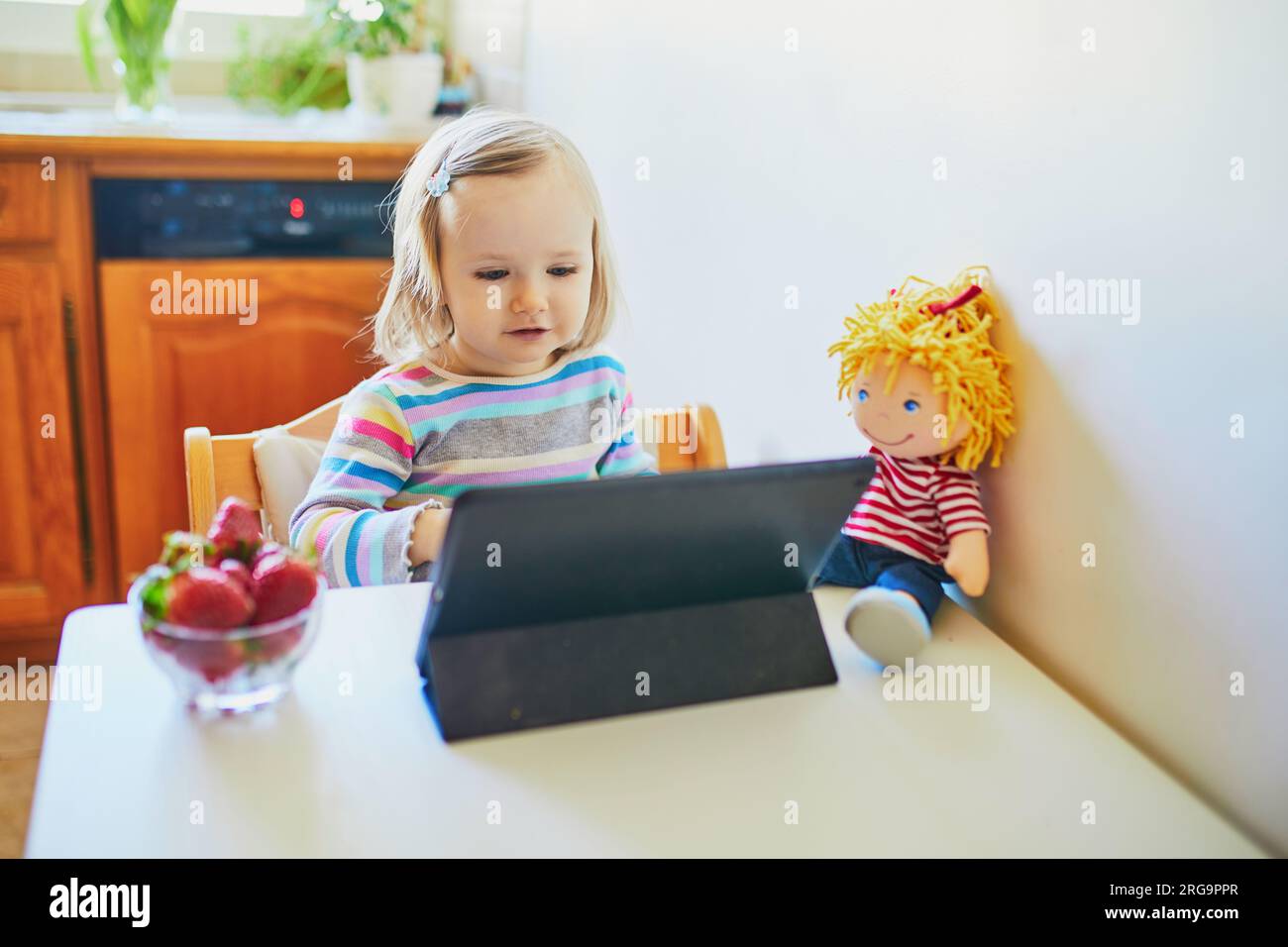 Adorable toddler girl eating fresh strawberries and using tablet. Child ...