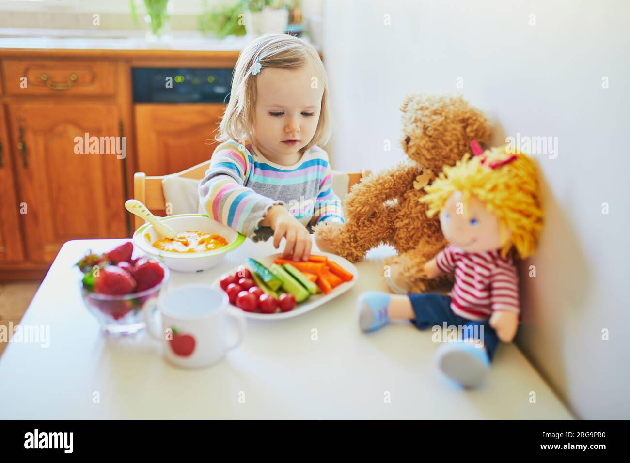 Adorable toddler girl eating fresh fruits and vegetables for lunch ...