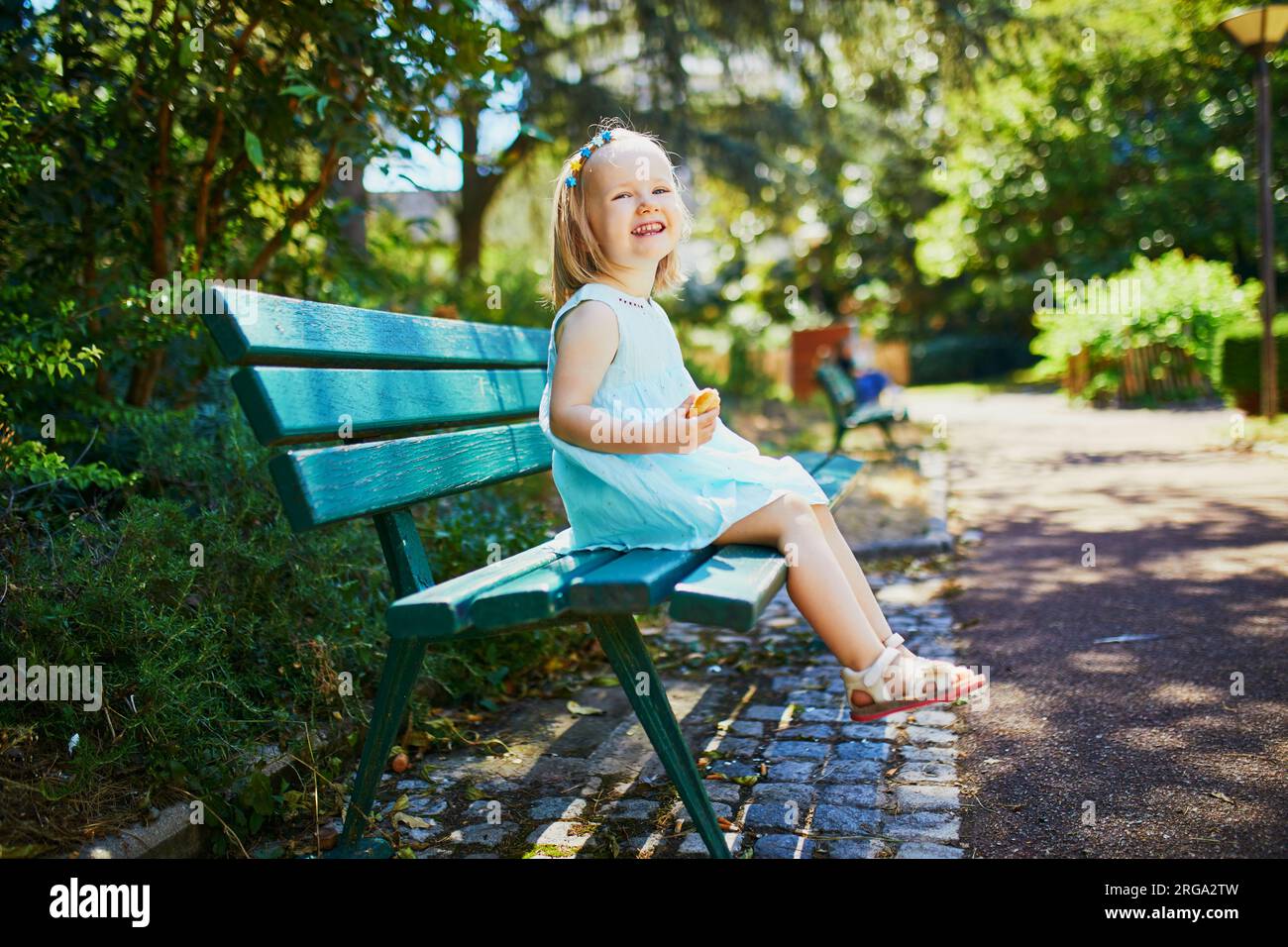 Adorable toddler girl sitting on the bench outdoors and having snack on ...