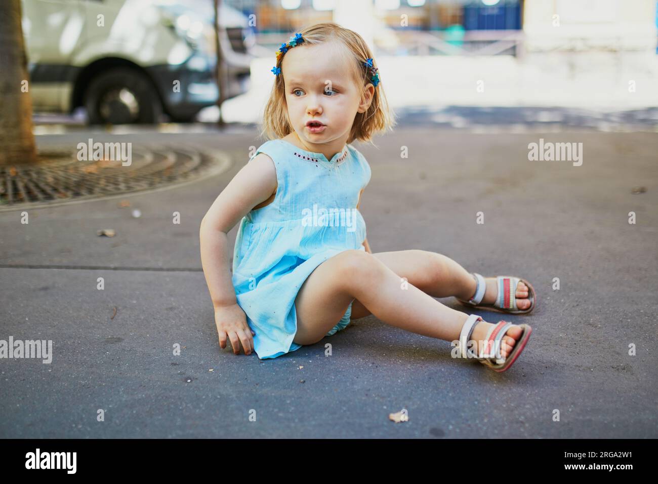 Unhappy and emotional toddler girl sitting on the floor outdoors ...