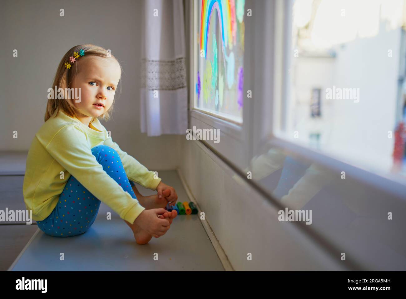 Adorable toddler girl drawing rainbow on window glass as sign of hope ...