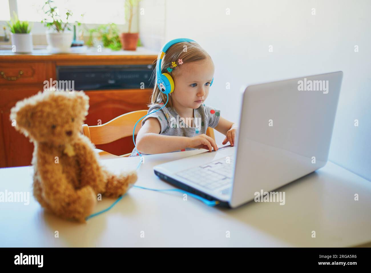Toddler girl wearing eraphones with laptop. Kid using computer to ...