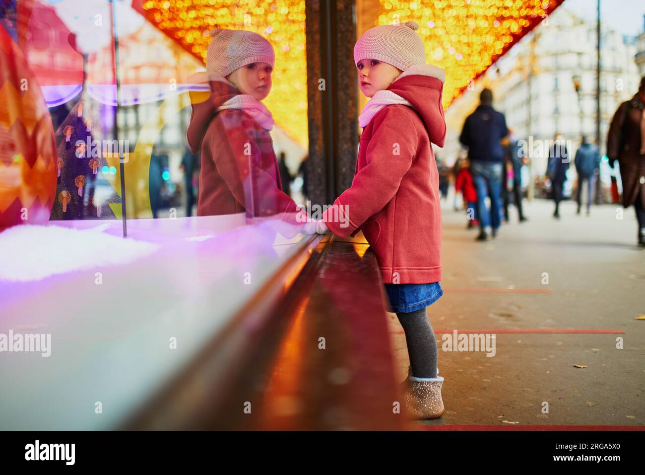 Toddler girl looking at window glass of large department store ...