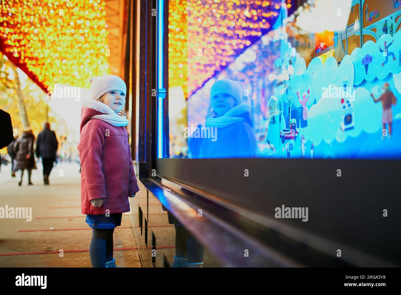 Toddler girl looking at window glass of large department store ...