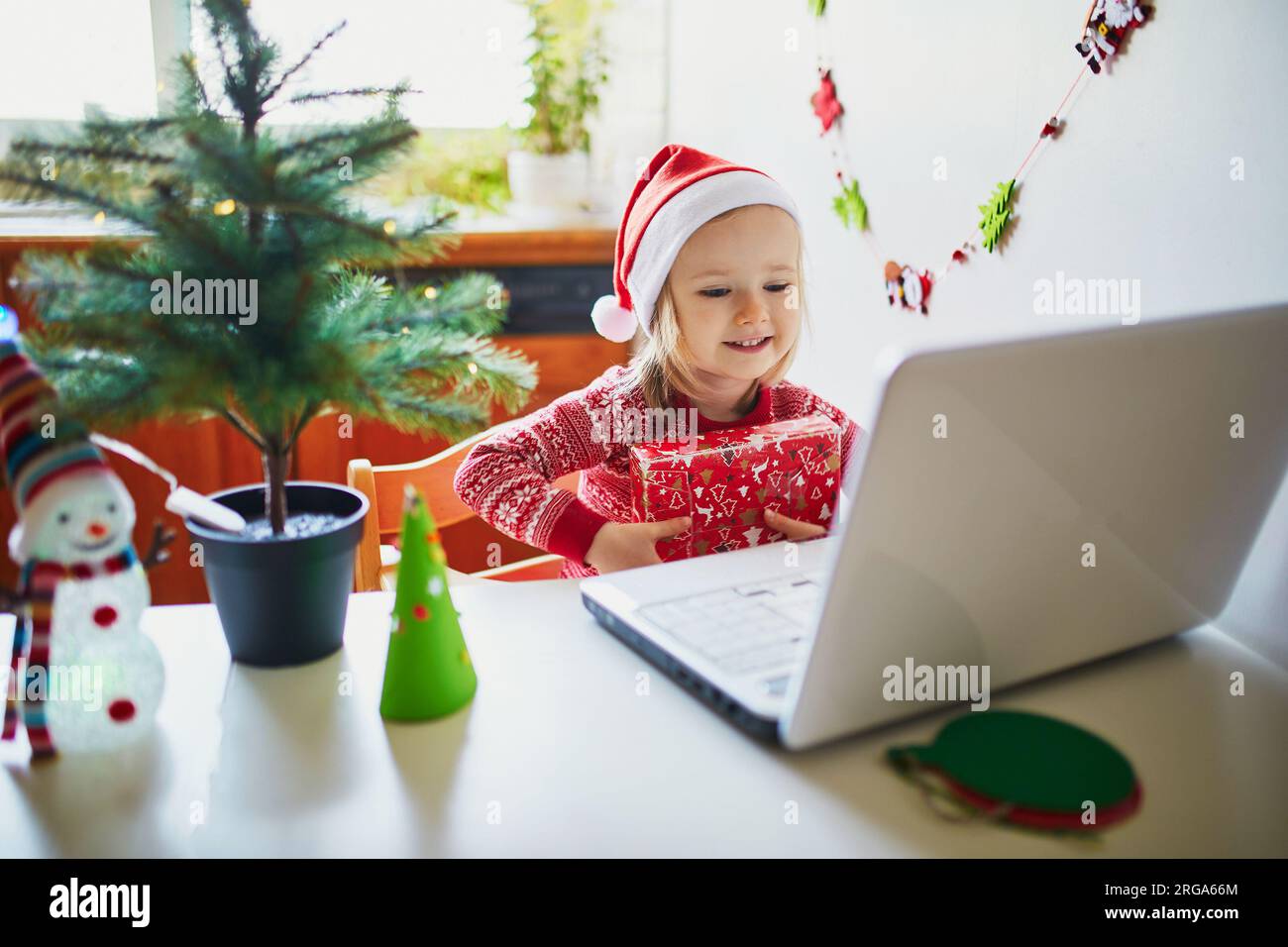 Happy toddler girl in Santa hat with present and laptop. Kid using ...