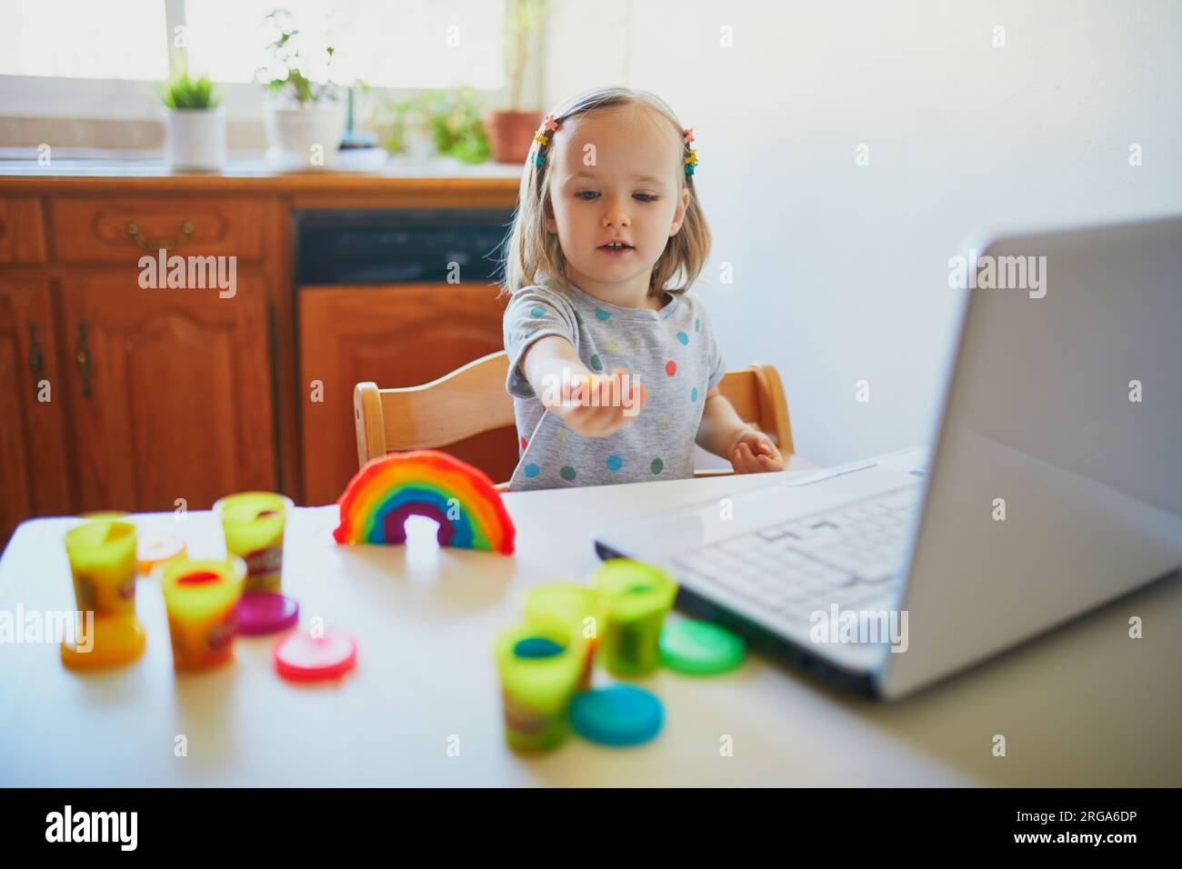 Toddler girl playing modelling clay in front of laptop. Kid using ...