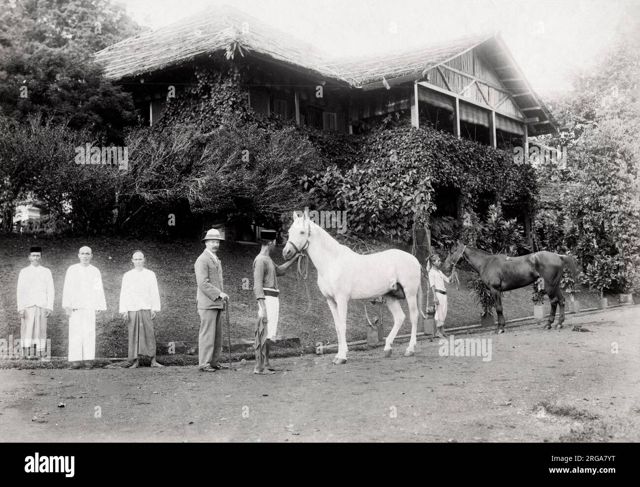 British man with his servants and horses outside his bungalow, late ...