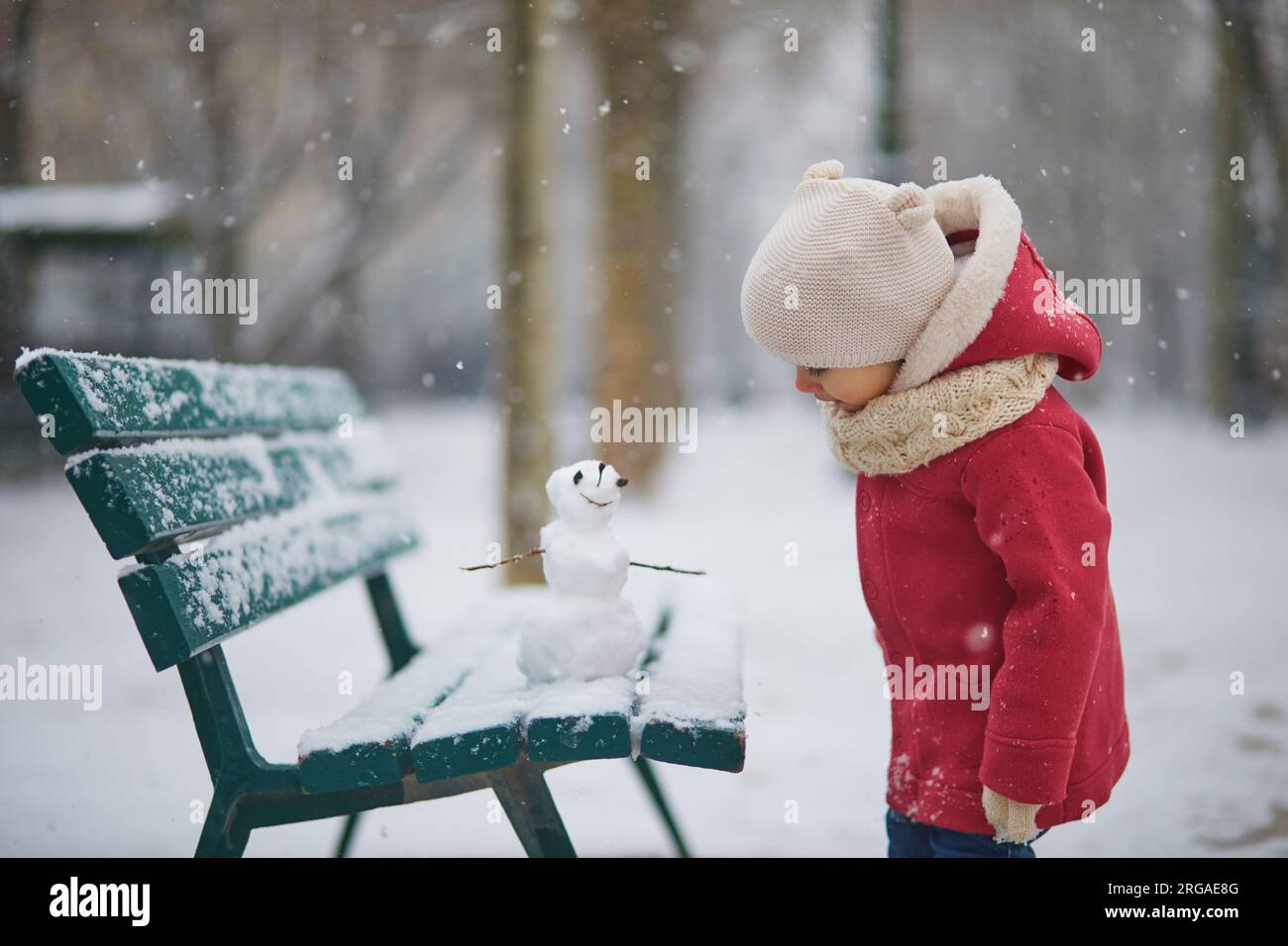 Adorable toddler girl building a snowman on a day with heavy snowfall ...