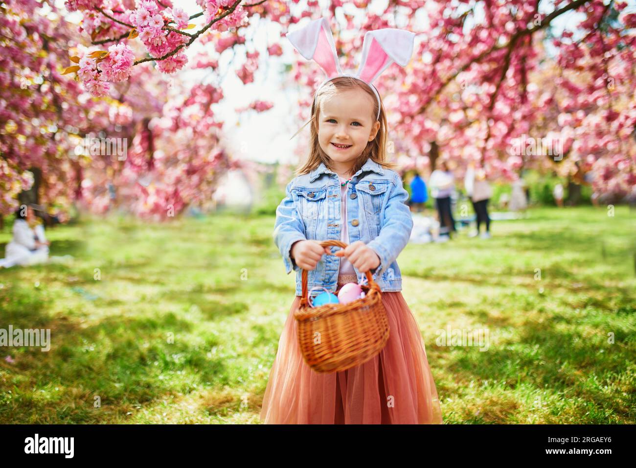 Preschooler girl wearing bunny ears playing egg hunt on Easter. Child ...