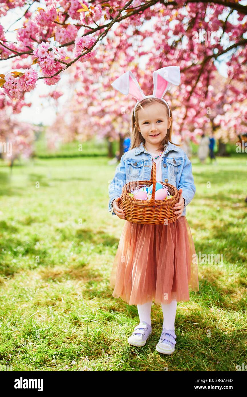 Preschooler girl wearing bunny ears playing egg hunt on Easter. Child ...
