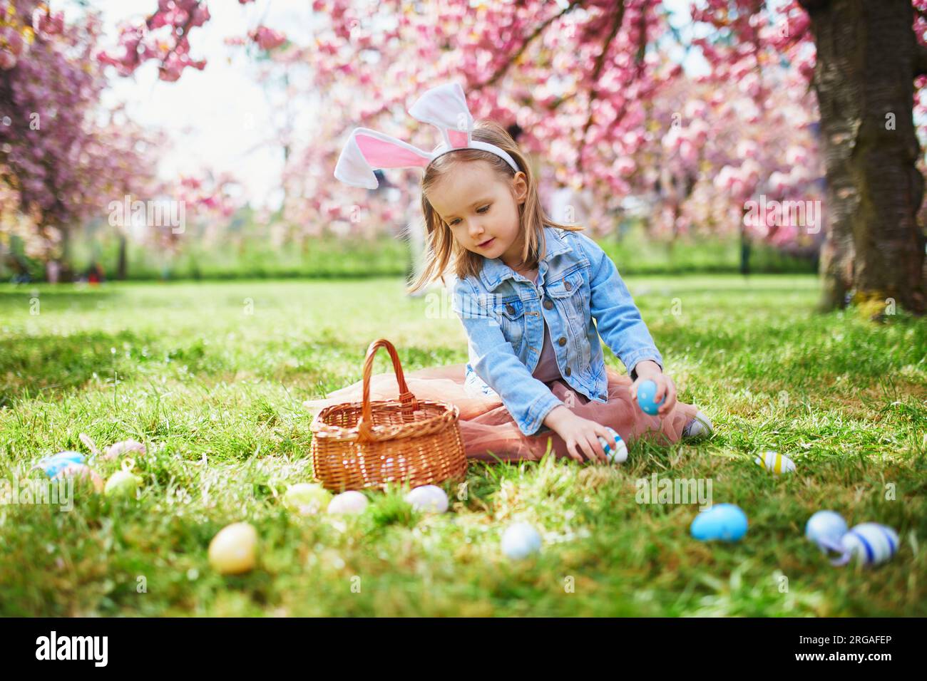 Preschooler girl wearing bunny ears playing egg hunt on Easter. Child ...