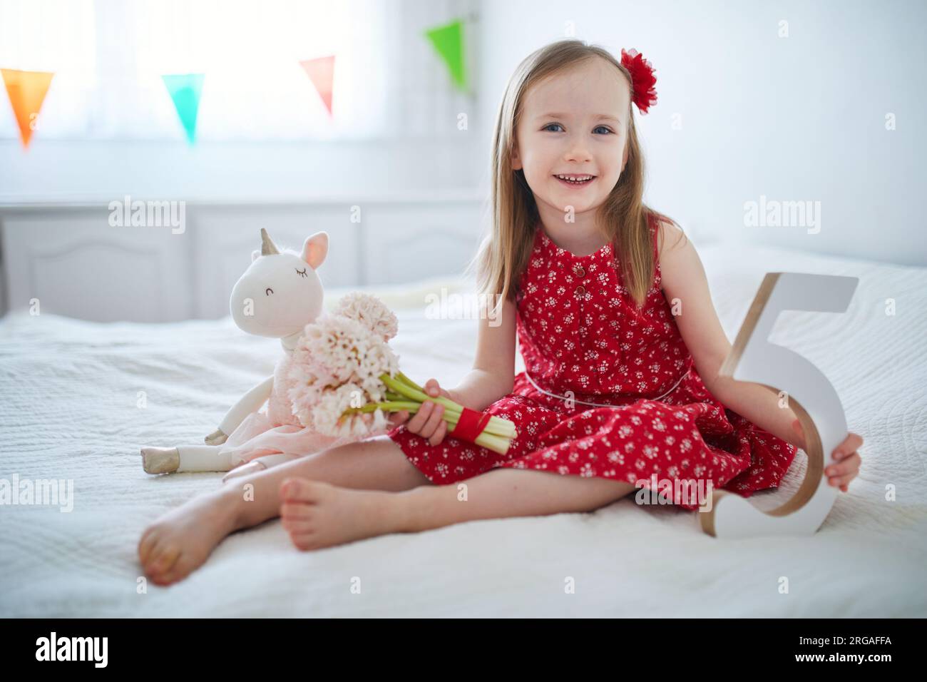 Adorable preschooler girl in red dress sitting on bed with pink ...
