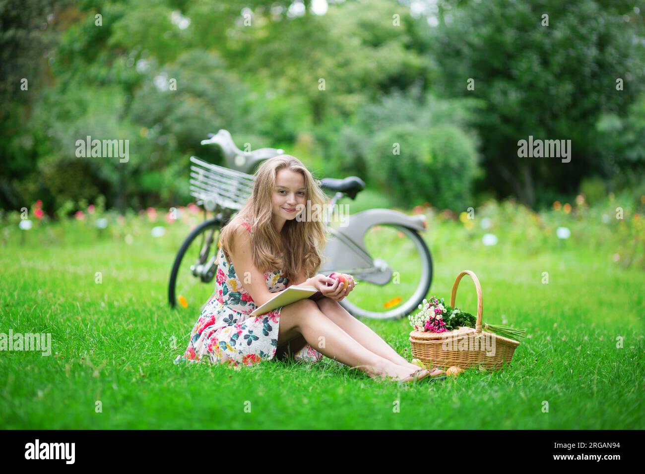 Beautiful young girl with bicycle in the countryside, reading a book ...