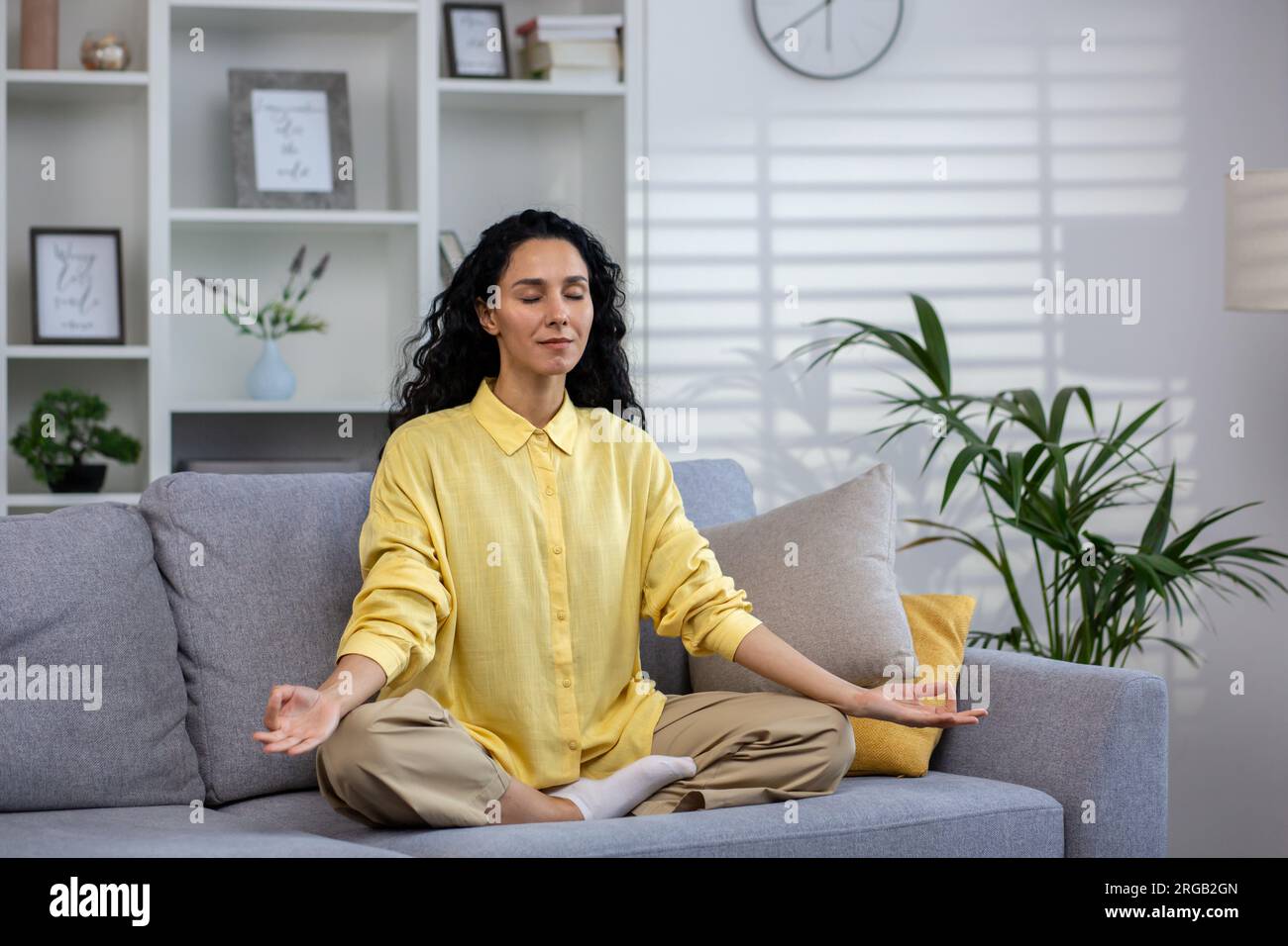 Young beautiful hispanic woman alone at home meditating sitting on sofa ...