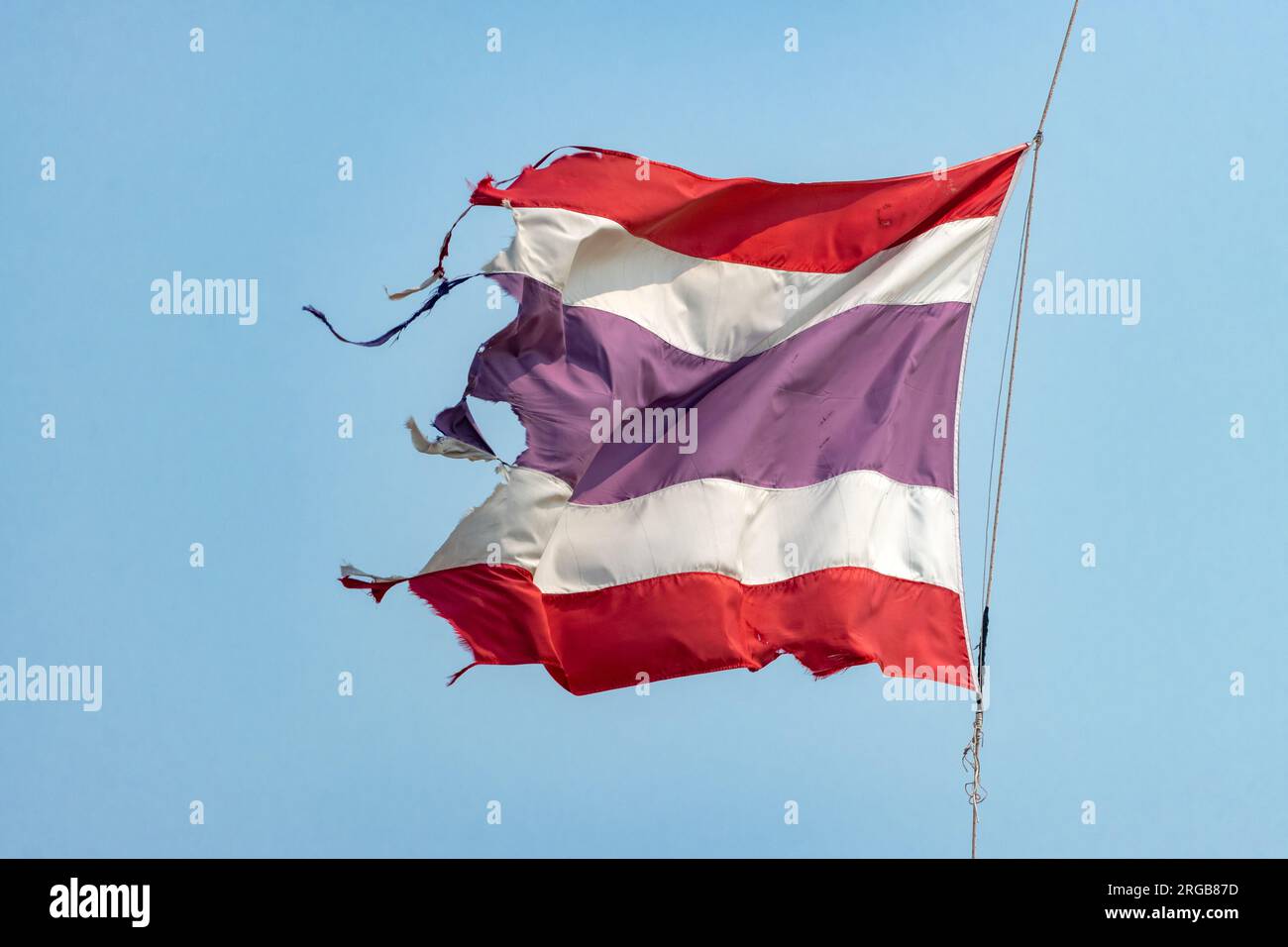 Torn national flag of Thailand flutters on a rope against a blue sky ...