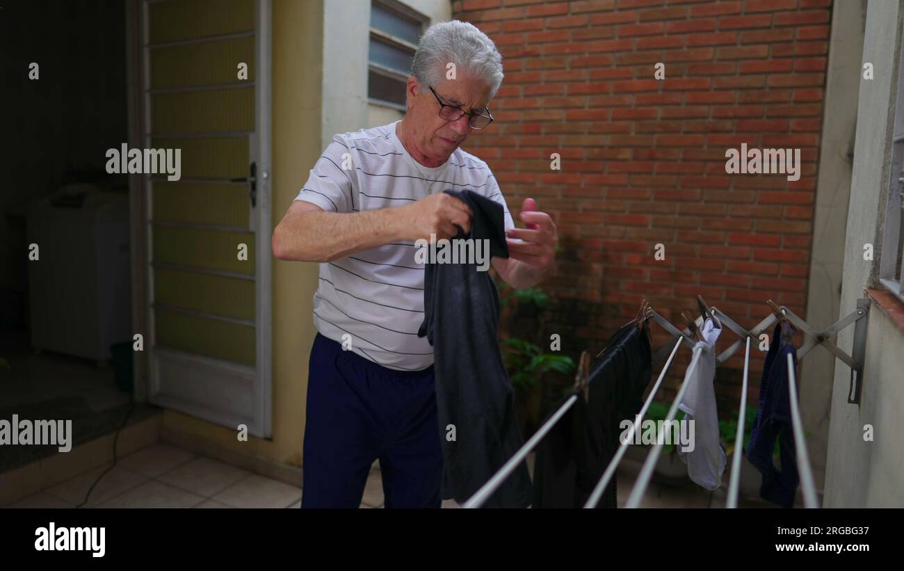 Senior man doing laundy and putting clothes to dry on hanger. Older ...