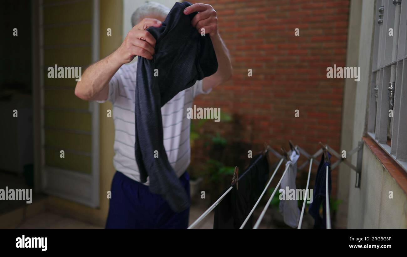 Senior man doing laundy and putting clothes to dry on hanger. Older ...