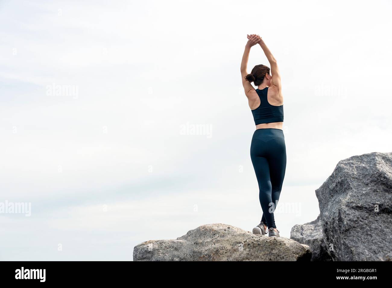 fit sporty woman doing a stretching exercise outside standing on rocks ...