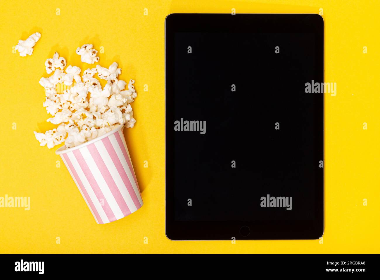 Popcorn bucket and blank black screen tablet on yellow background. Top ...