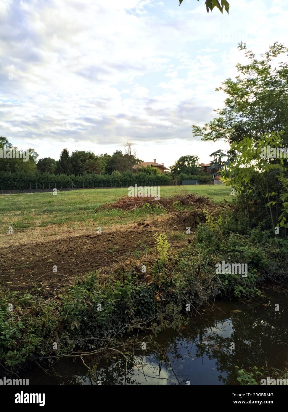 Field and houses bordered by a trench with water and trees at sunset in ...
