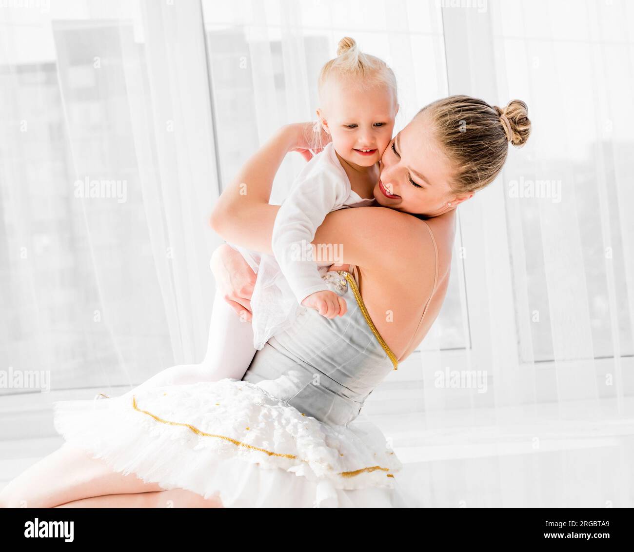 Young mother in swan ballet dress hugging little smiling daughter ...