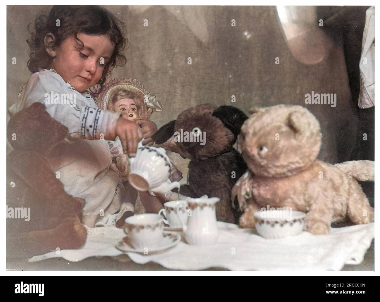 A little girl hosts a tea party - three bears and a doll attend Stock ...