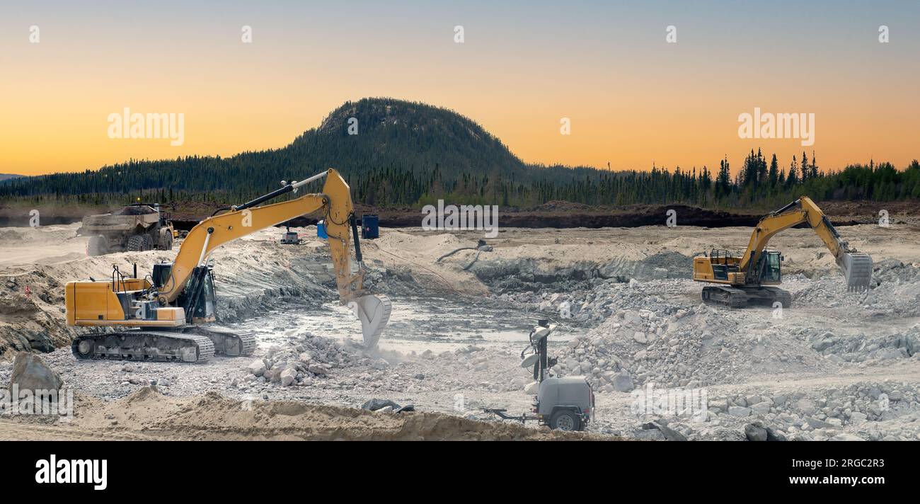 Excavators placing stones in an excavation at sunset with a mountain in ...