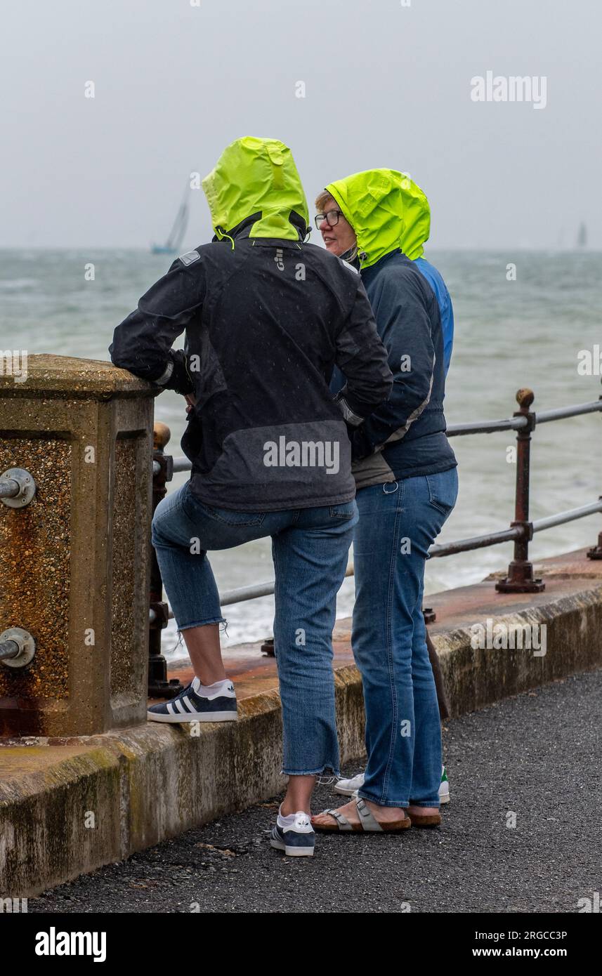 two people wearing sailing clothing in the poring rain on a wet day at ...