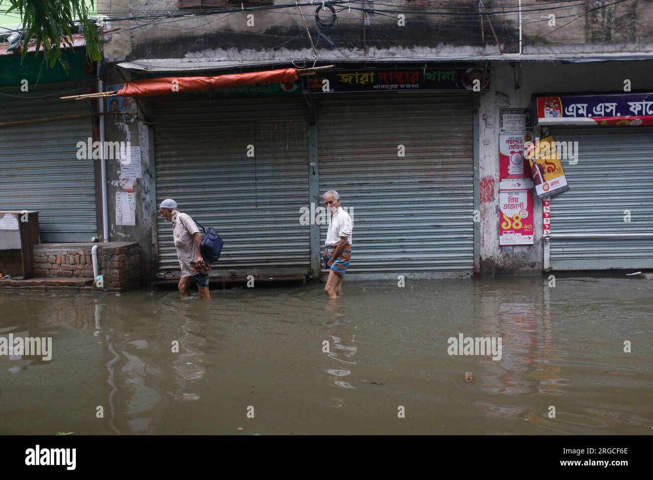 DHAKA, BANGLADESH- AUGUST 7, 2023: Residents walk through flooded street after heavy rainfall in ...