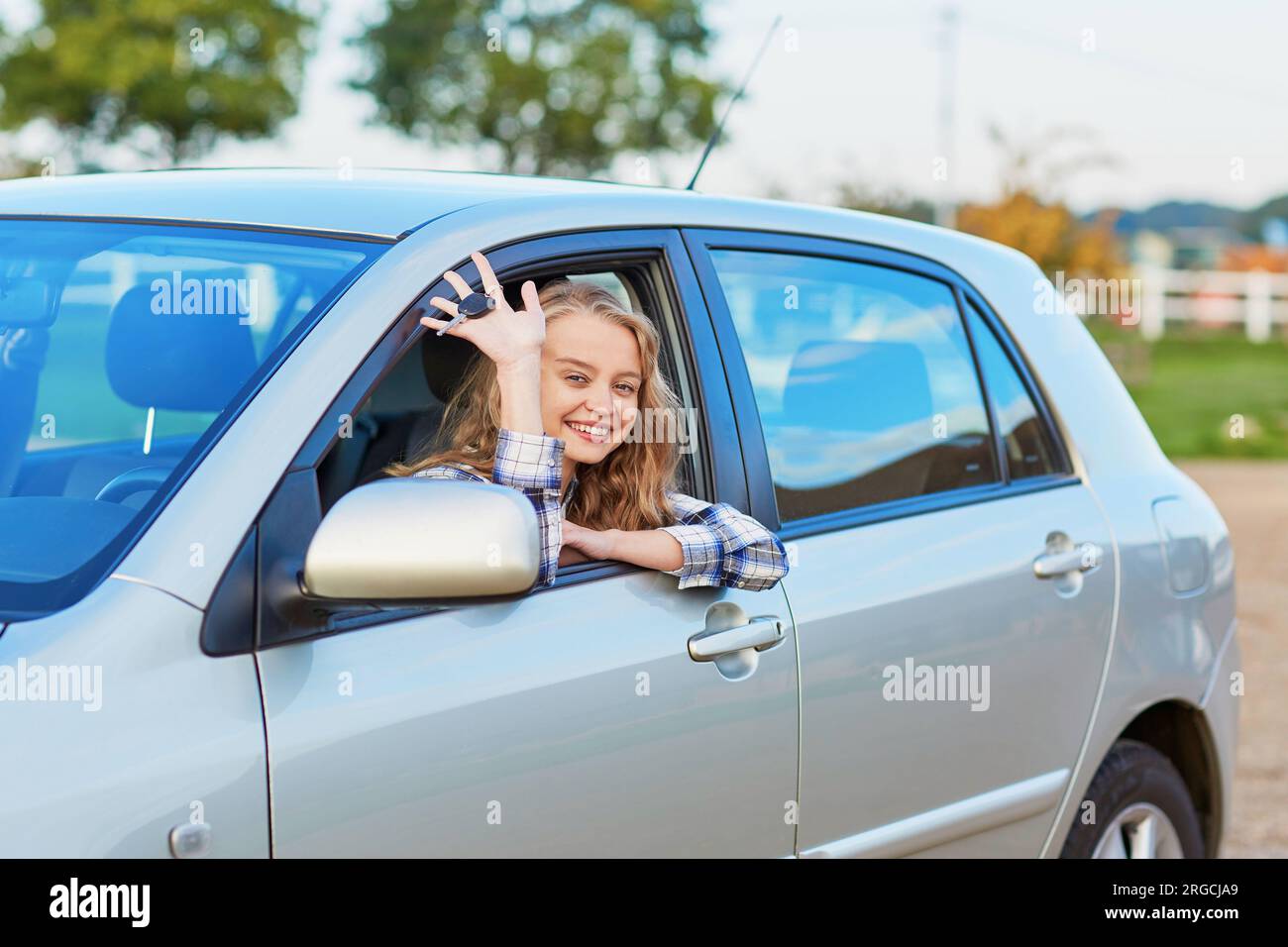 Beautiful young driver looking out of the car window holding a key ...