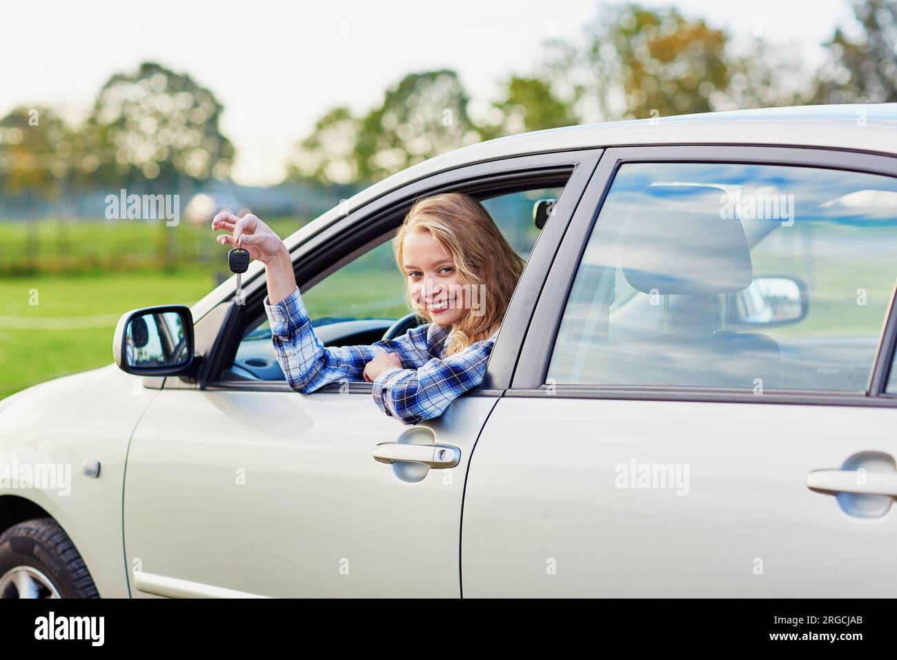 Beautiful young driver looking out of the car window holding a key ...