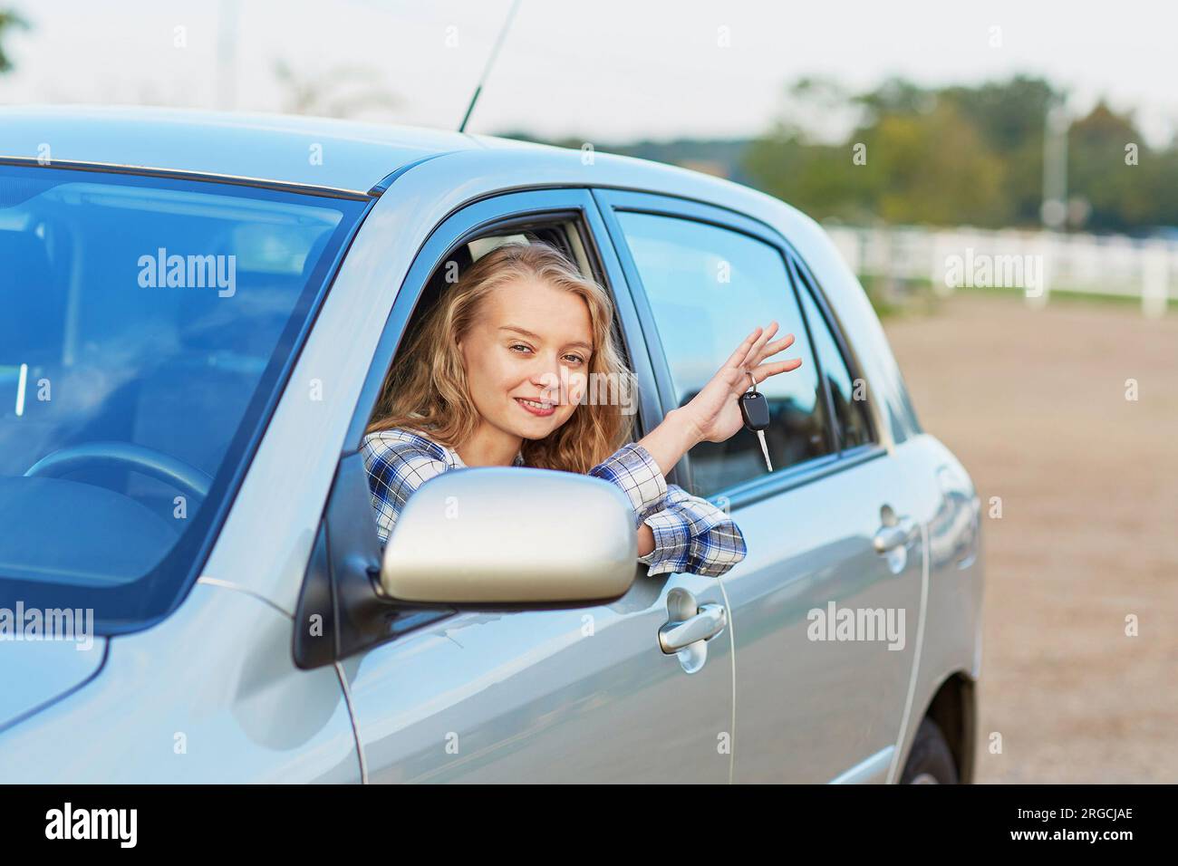 Beautiful young driver looking out of the car window holding a key ...