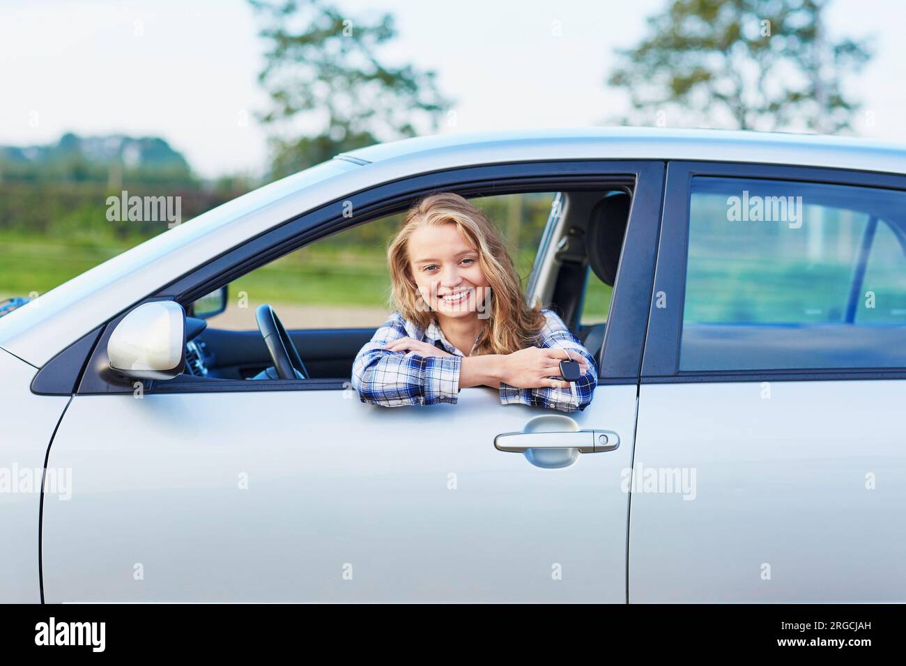 Beautiful young driver looking out of the car window holding a key ...