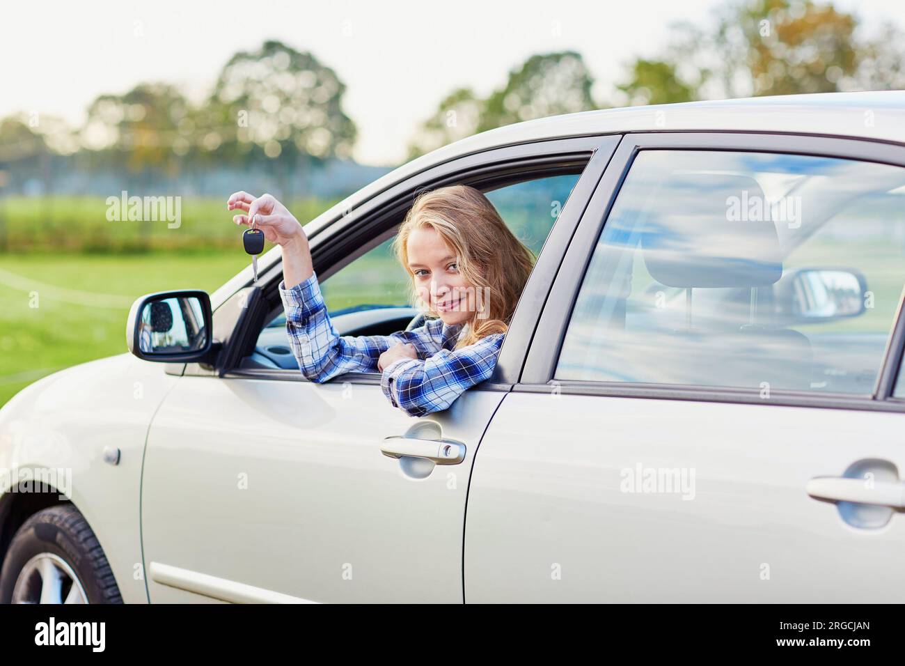 Beautiful young driver looking out of the car window holding a key ...