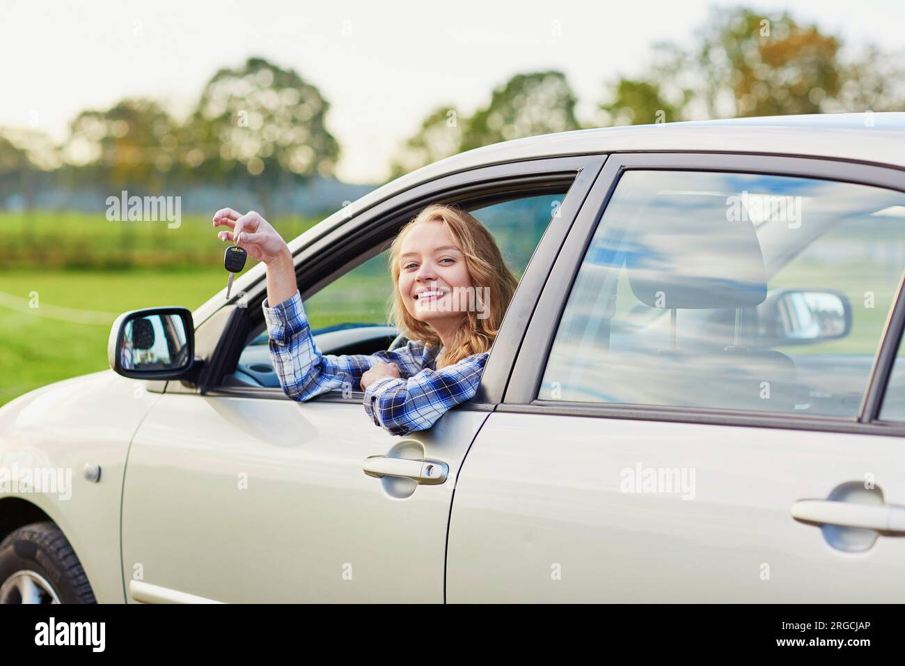 Beautiful young driver looking out of the car window holding a key ...