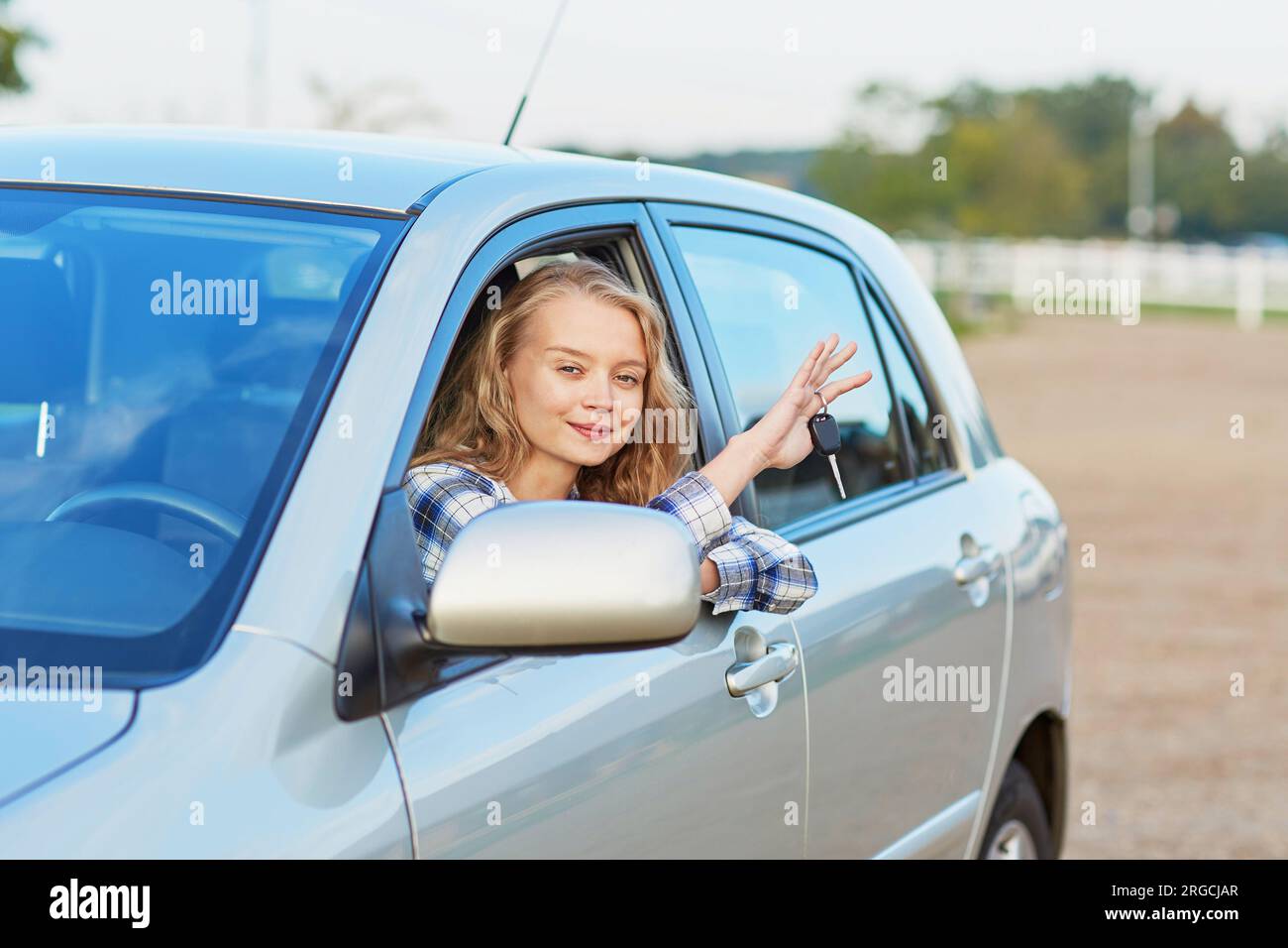 Beautiful young driver looking out of the car window holding a key ...